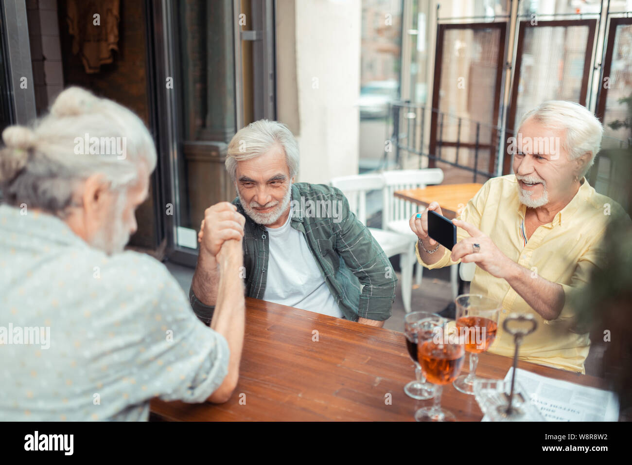 Grey-haired bearded man filming his friends arm-wrestling Stock Photo ...