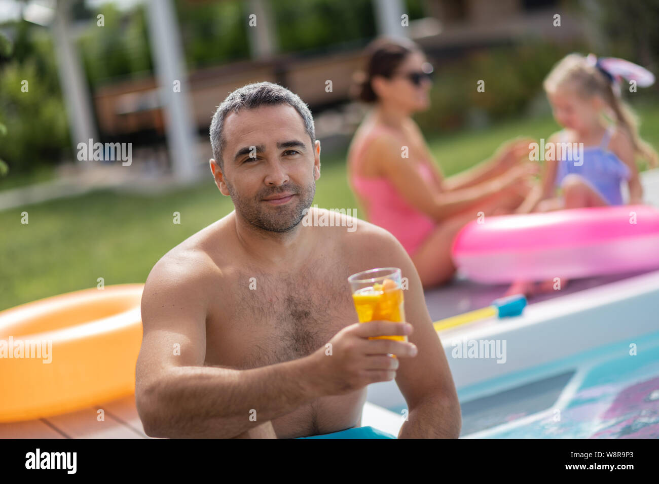 Man drinking cold cocktail while chilling with family near pool Stock ...