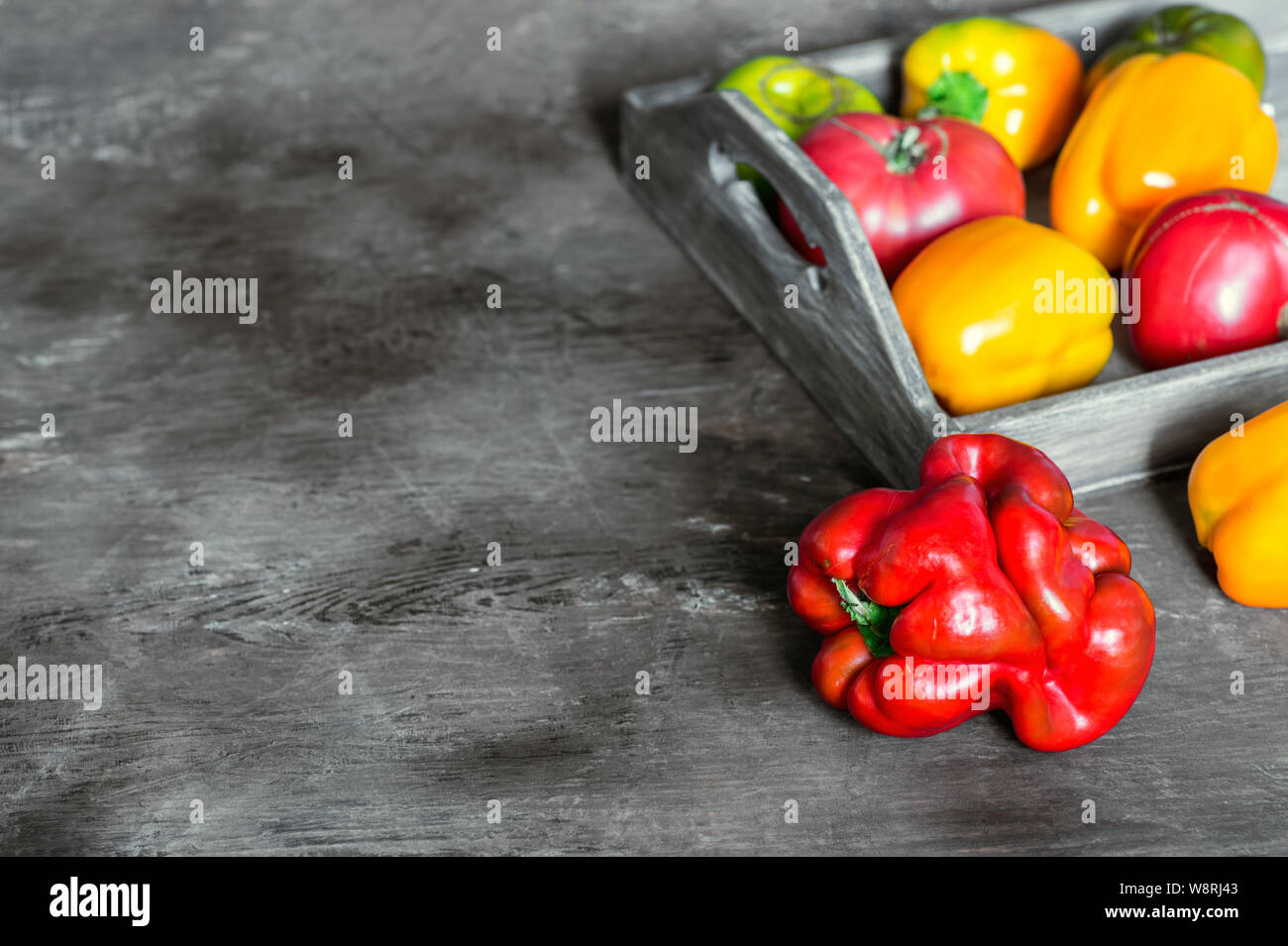 Imperfect natural peppers and tomatoes on an old wooden tray on a dark ...