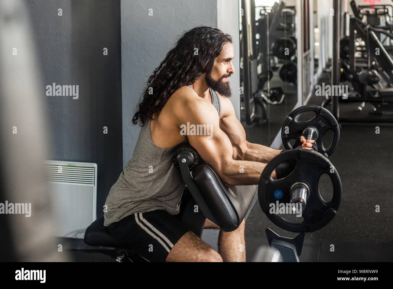 Side view portrait of young adult bodybuilder with long curly hair are ...