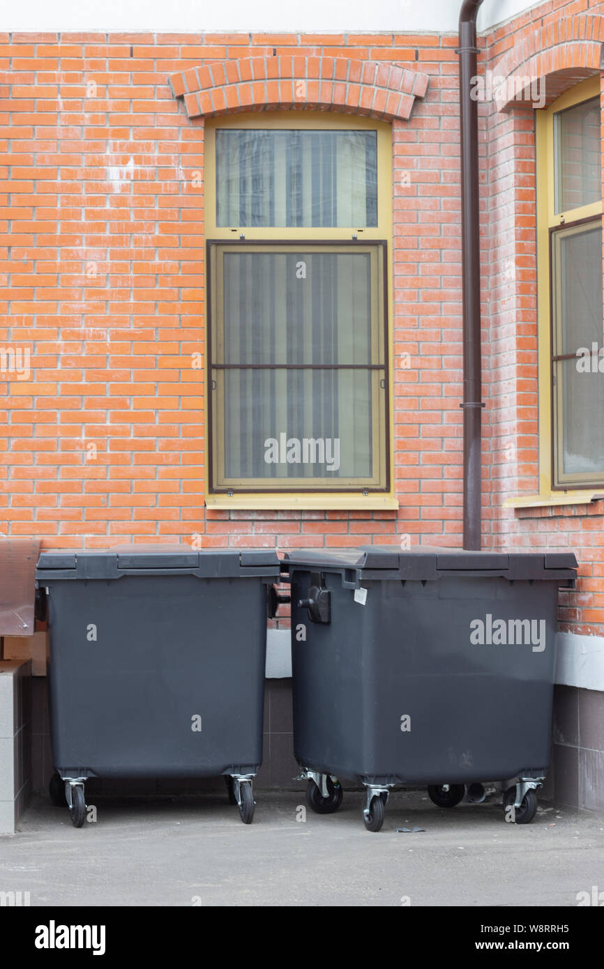 Two black waste trash containers under the windows of a brick building ...
