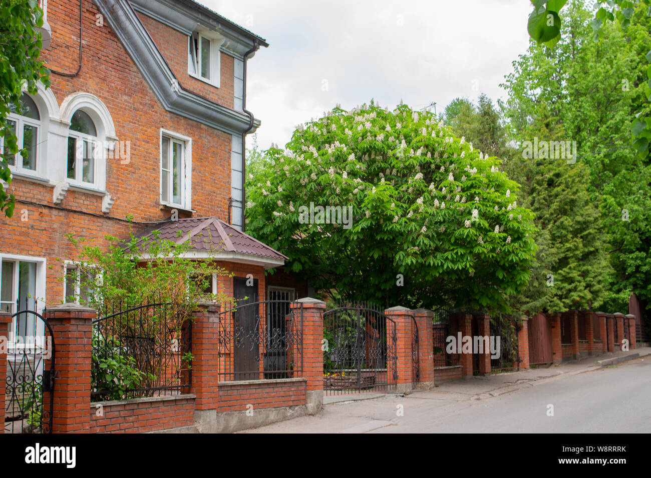 Beautiful courtyard with a brick red house, forged gates and lush ...