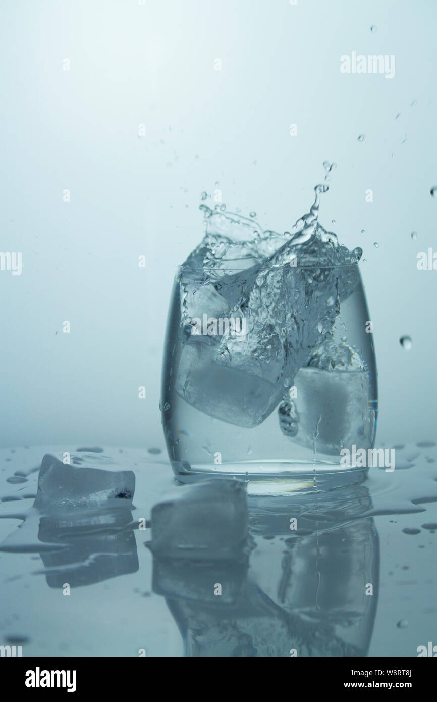 Ice falling with a splash in a transparent glass with water. Pure ...