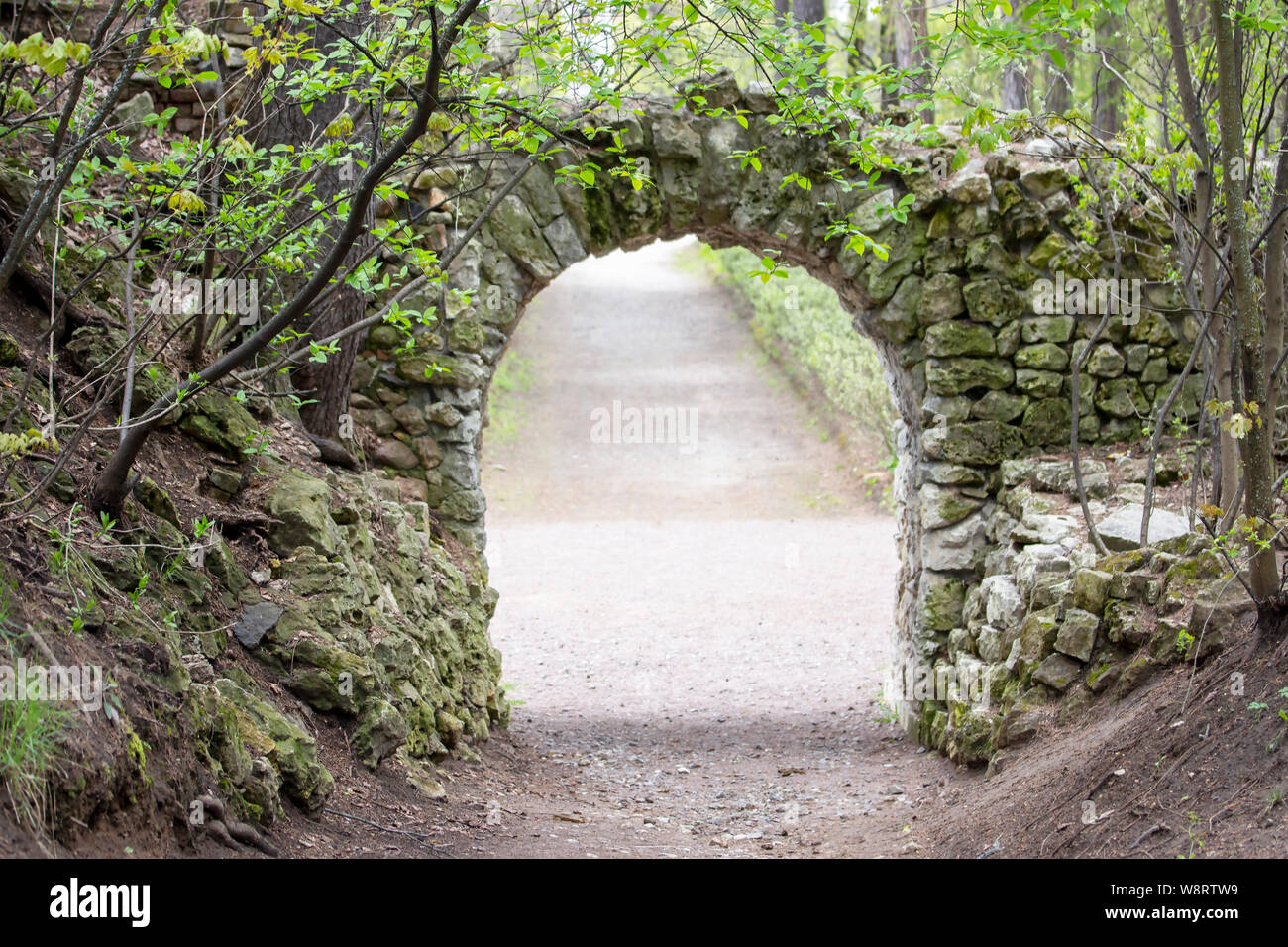 ancient stone arch overgrown with moss. Path leading to stone wall ...