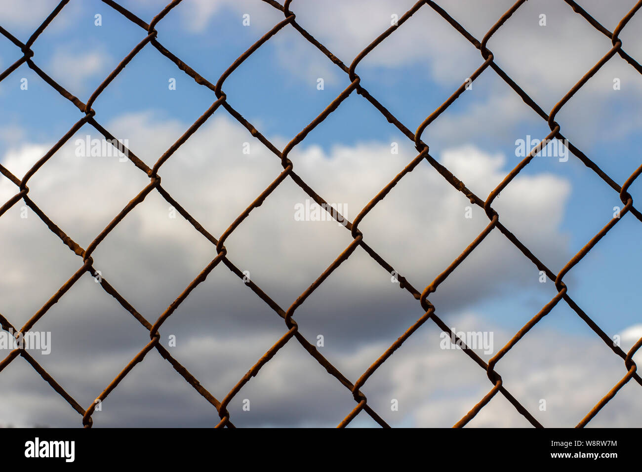 Old rusty mesh netting on a blue sky with clouds, background wallpaper ...