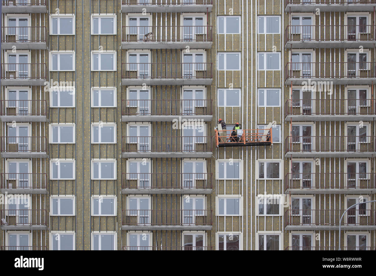 Two builders in helmets hang in a basket on the wall of an unfinished ...