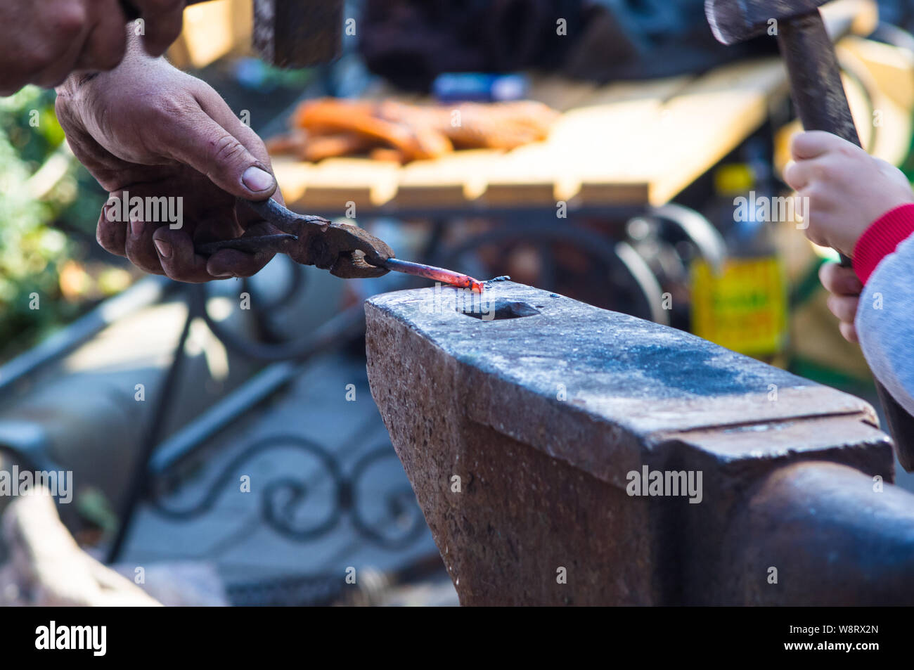 blacksmith performs the forging of hot glowing metal on the anvil ...