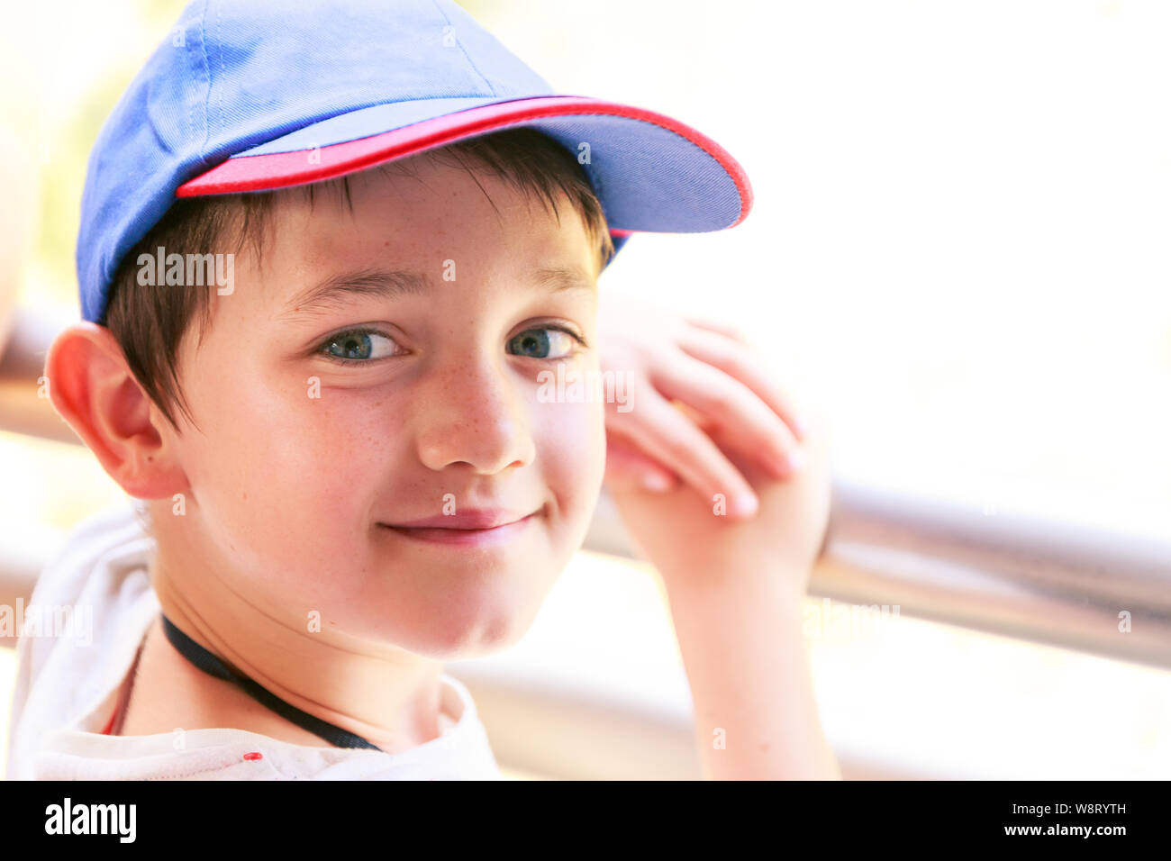 Cheerful 8 year old boy wearing blue baseball hat turns face to camera ...