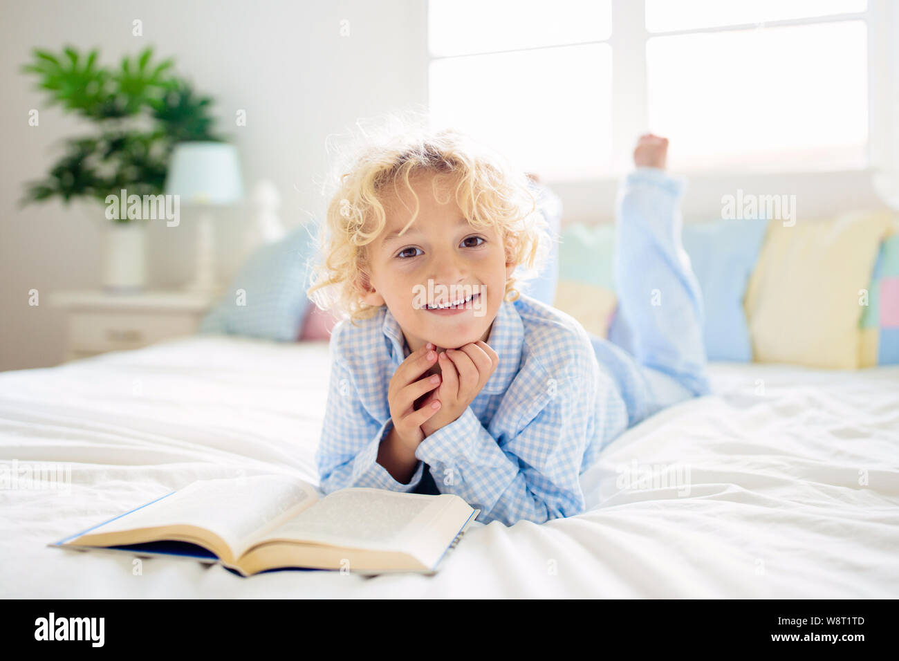 Child reading book in bed in white sunny bedroom with window. Children ...