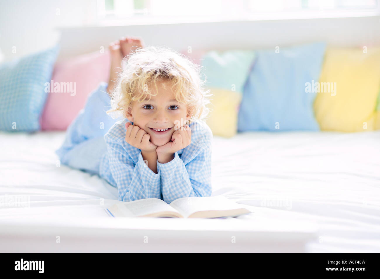 Child reading book in bed in white sunny bedroom with window. Children ...