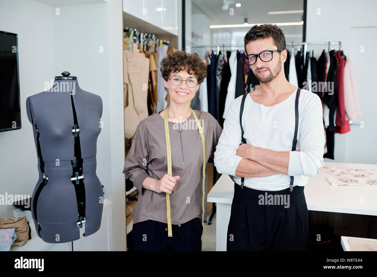 Two happy young creative designers of clothing standing by mannequin ...