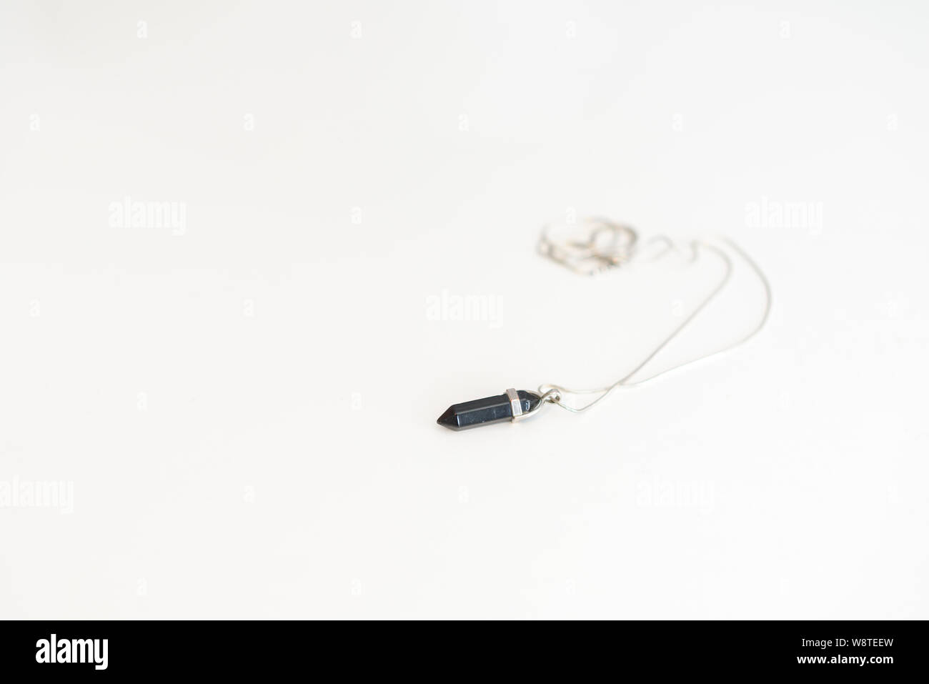 Close up of black pendulum on silver chain on white table. Foretelling ...