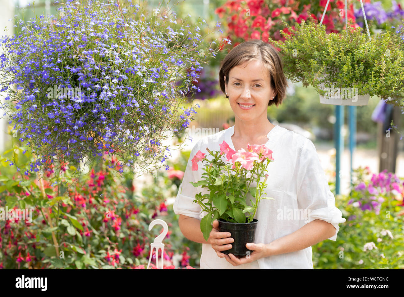 Pretty female garden center staff with bunch of petunias in hands Stock ...