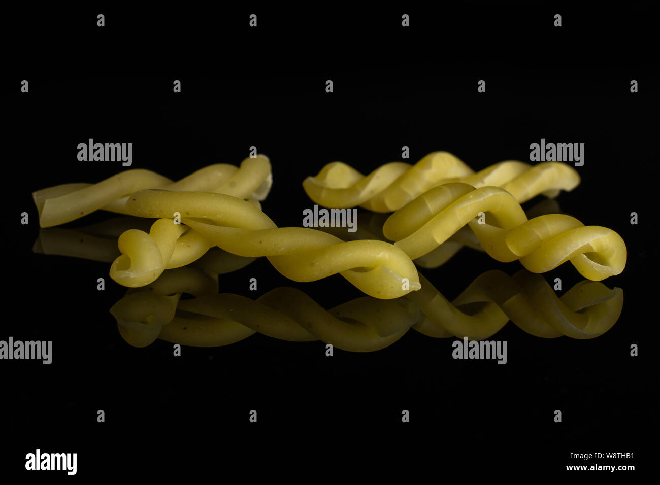 Group of five whole raw pasta gemelli isolated on black glass Stock ...