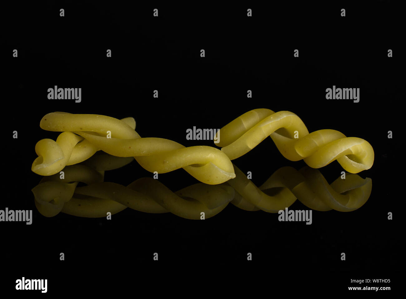 Group of three whole raw pasta gemelli isolated on black glass Stock ...