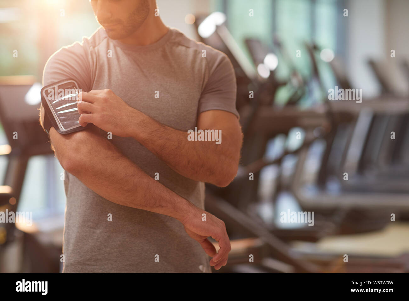 Mid-section portrait of muscular man checking smartphone in arm holder ...