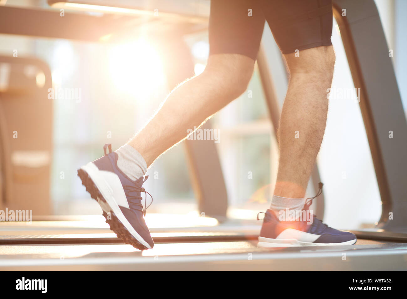 Sports background of muscular male legs running on treadmill in gym lit ...