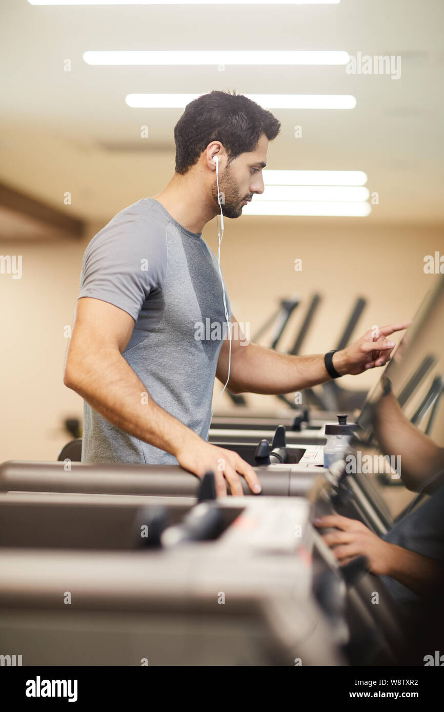 Side view portrait of handsome young man running on treadmill in gym ...
