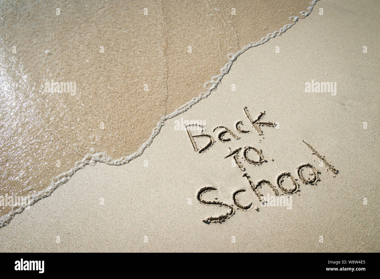 Back to School message handwritten on smooth sand beach with incoming ...