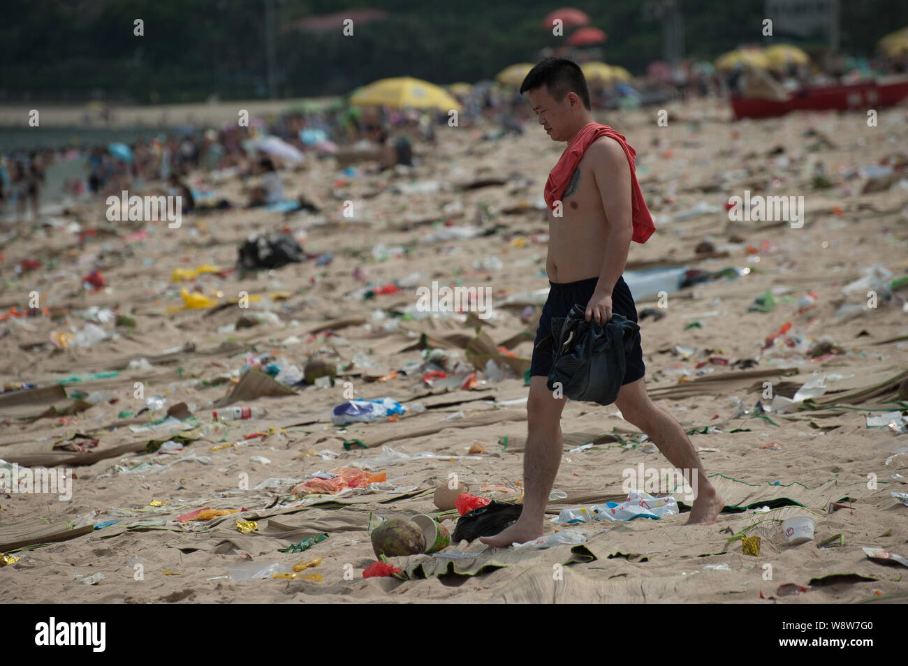 A Chinese holidaymaker walks across the beach strewn with garbage at ...