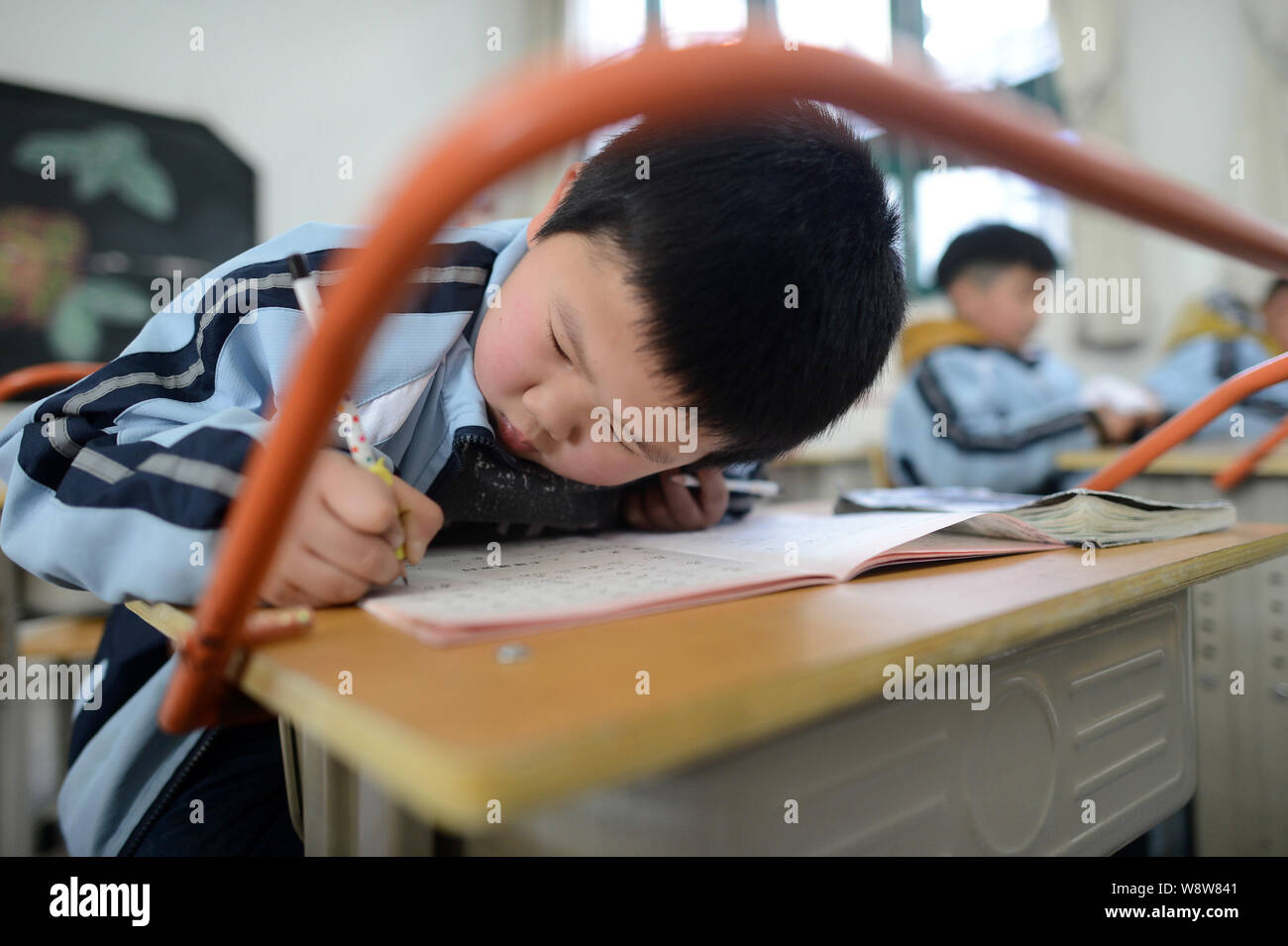 A Chinese schoolboy writes his homework on a desk with a bar installed ...