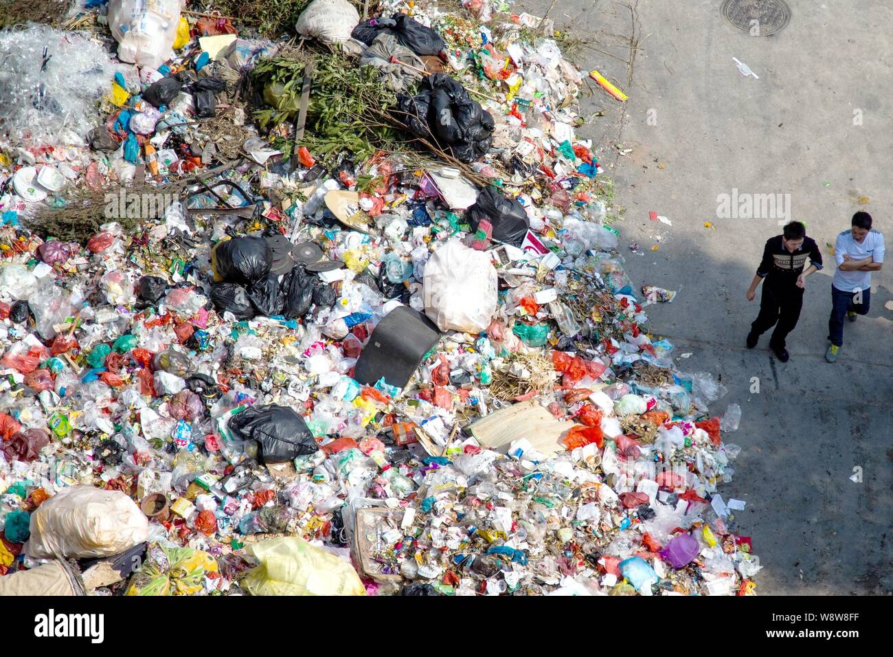 Chinese pedestrians walk past piles of garbage left on a road in Shiyan ...