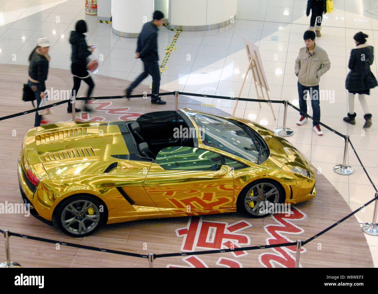 Shoppers look at a golden convertible Lamborghini sports car on display ...