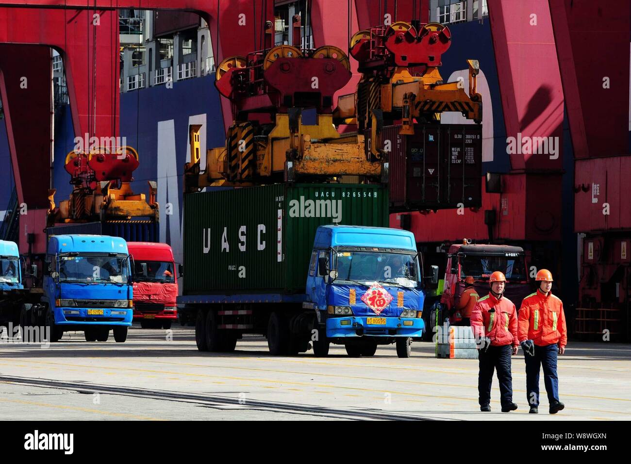 --FILE--Chinese workers walk past container trucks being loaded on a ...