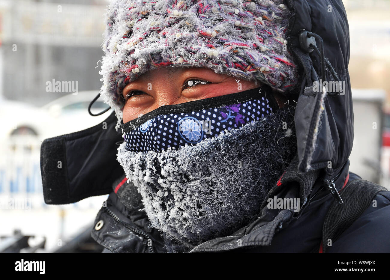 A pedestrian wearing a face mask and a hat against a cold front is ...