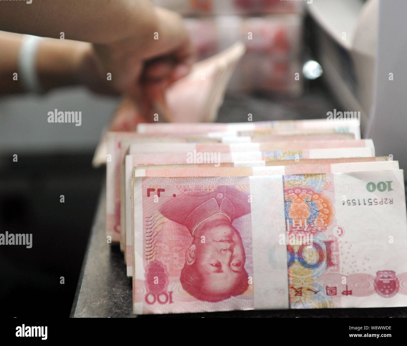 A Chinese clerk counts RMB (renminbi) yuan banknotes at a branch of the ...