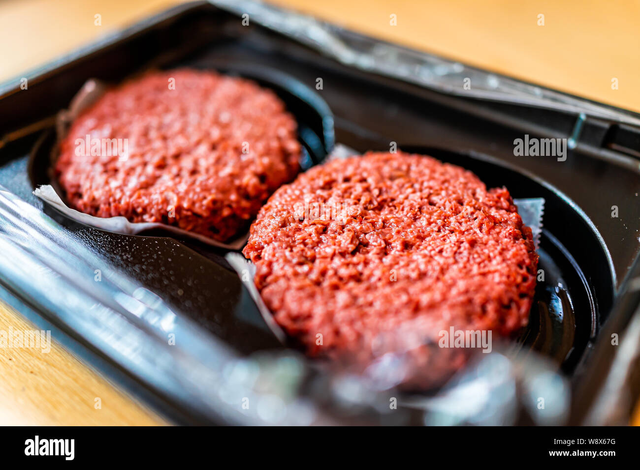 Closeup of two raw uncooked red vegan meat burger patties in plastic ...