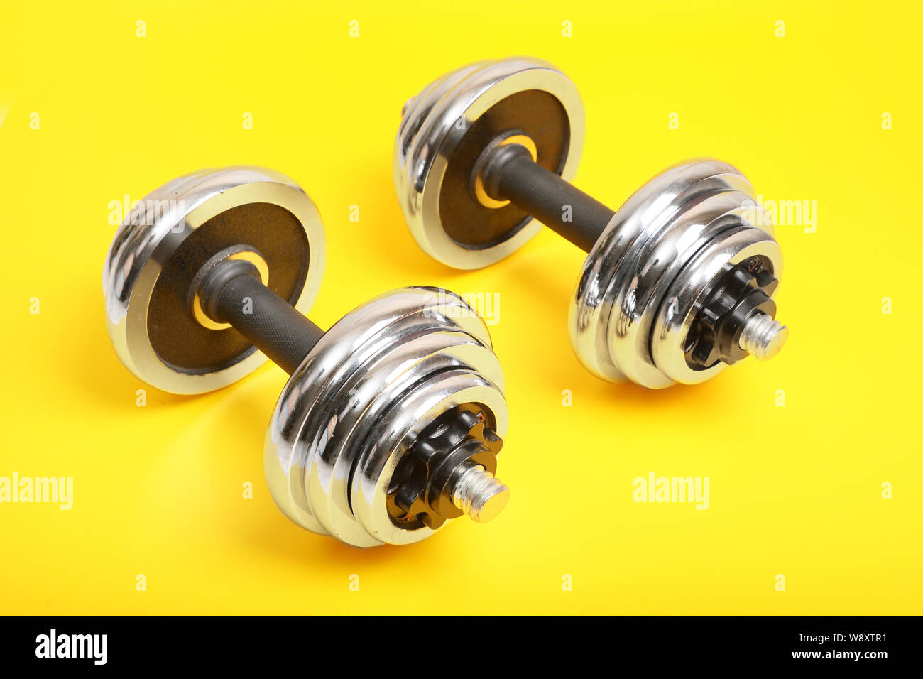 A pair of steel heavy dumbbells, on a bright yellow background Stock ...
