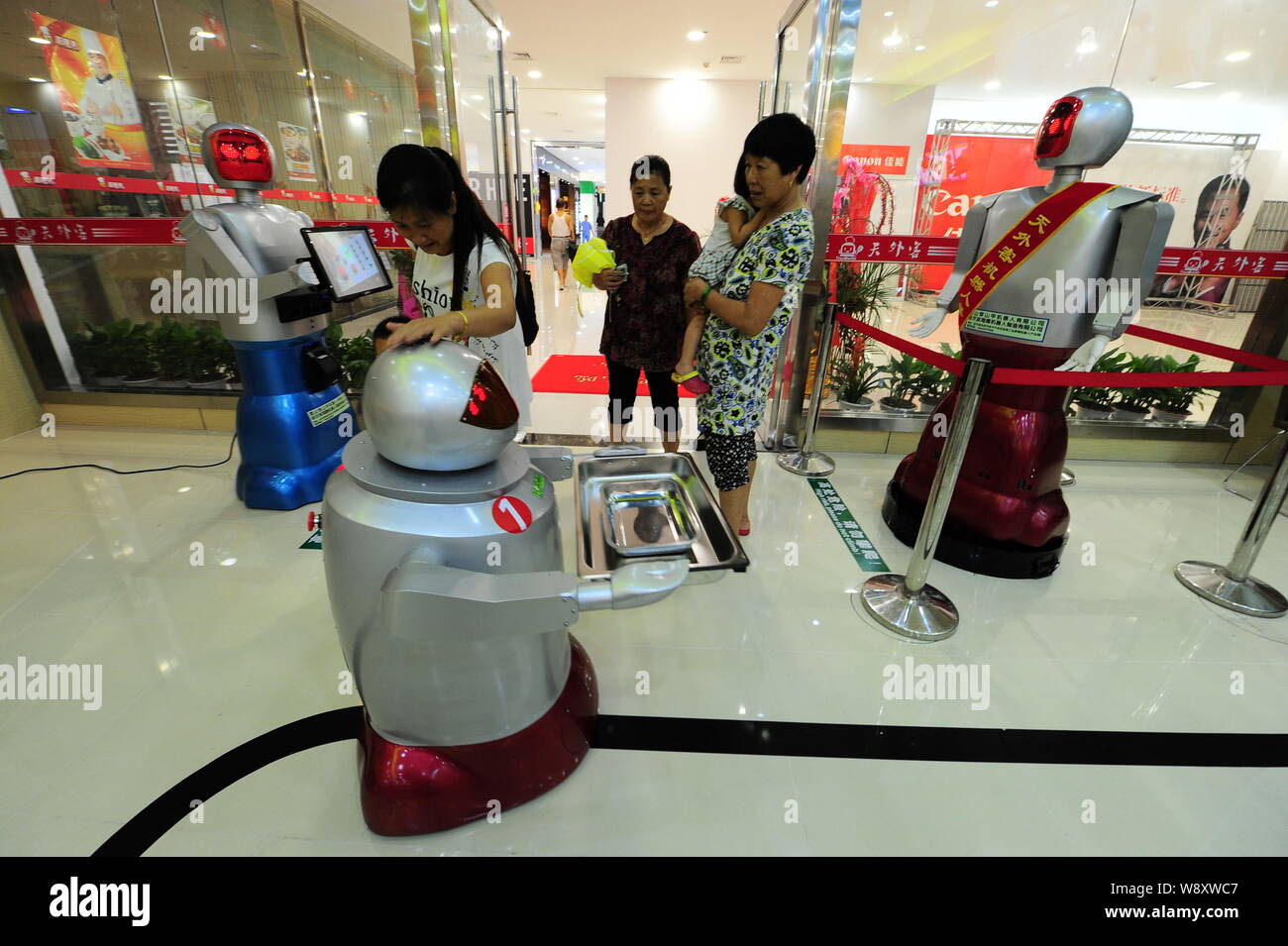 Two standing robots welcome customers as the third is delivering dishes ...
