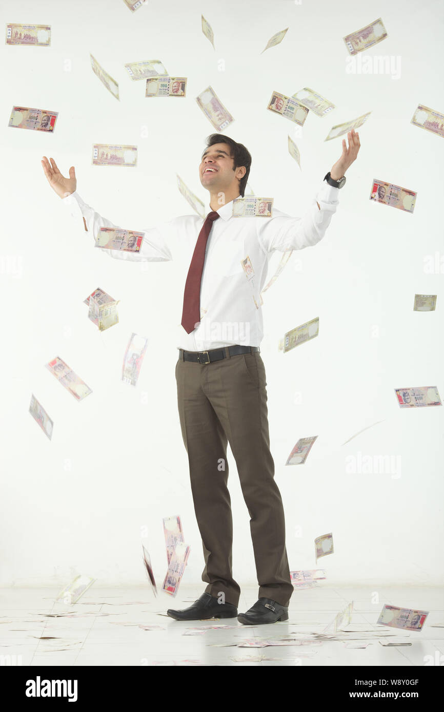 Money falling on a businessman standing with his arms outstretched ...