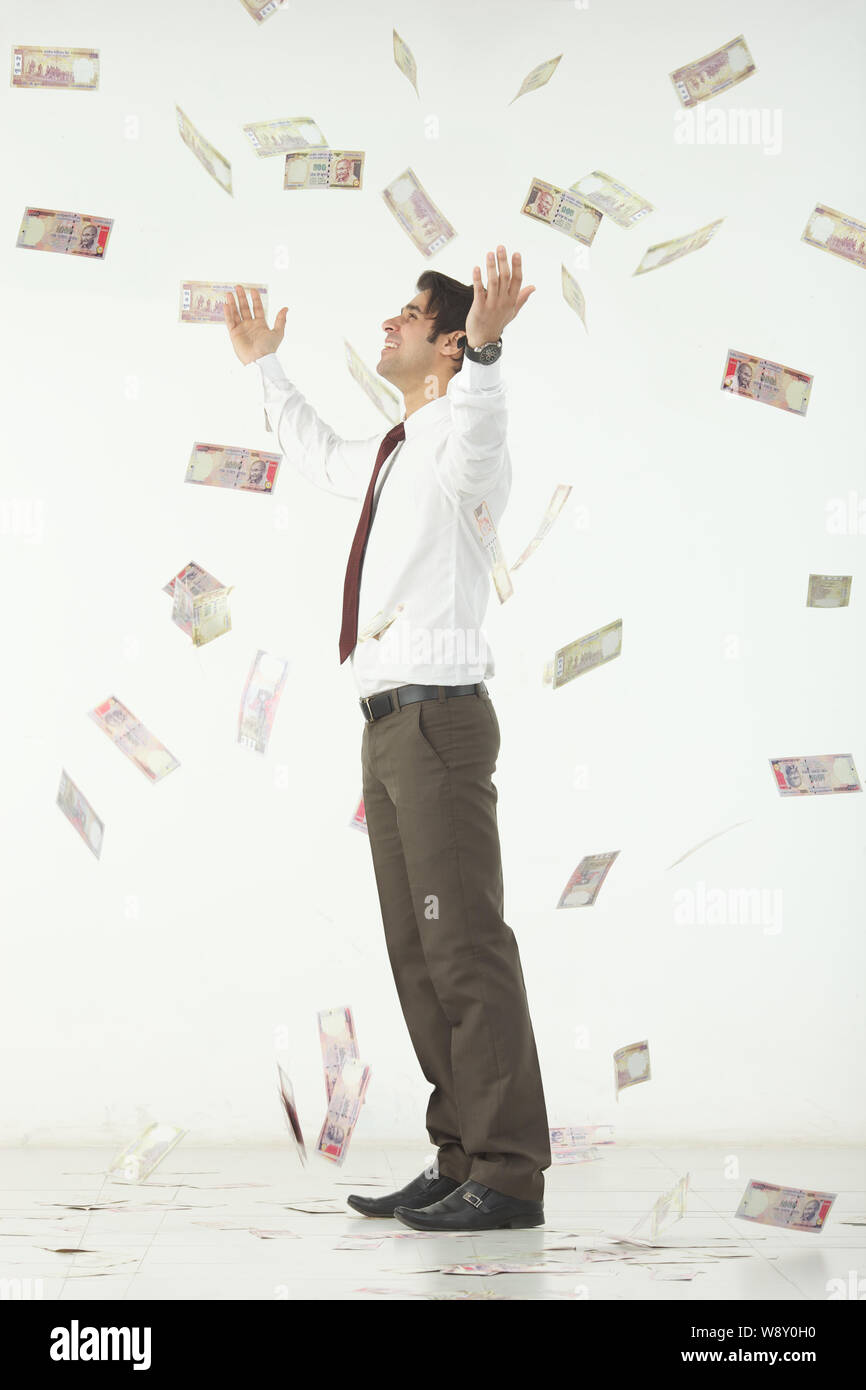 Money falling on a businessman standing with his arms outstretched ...