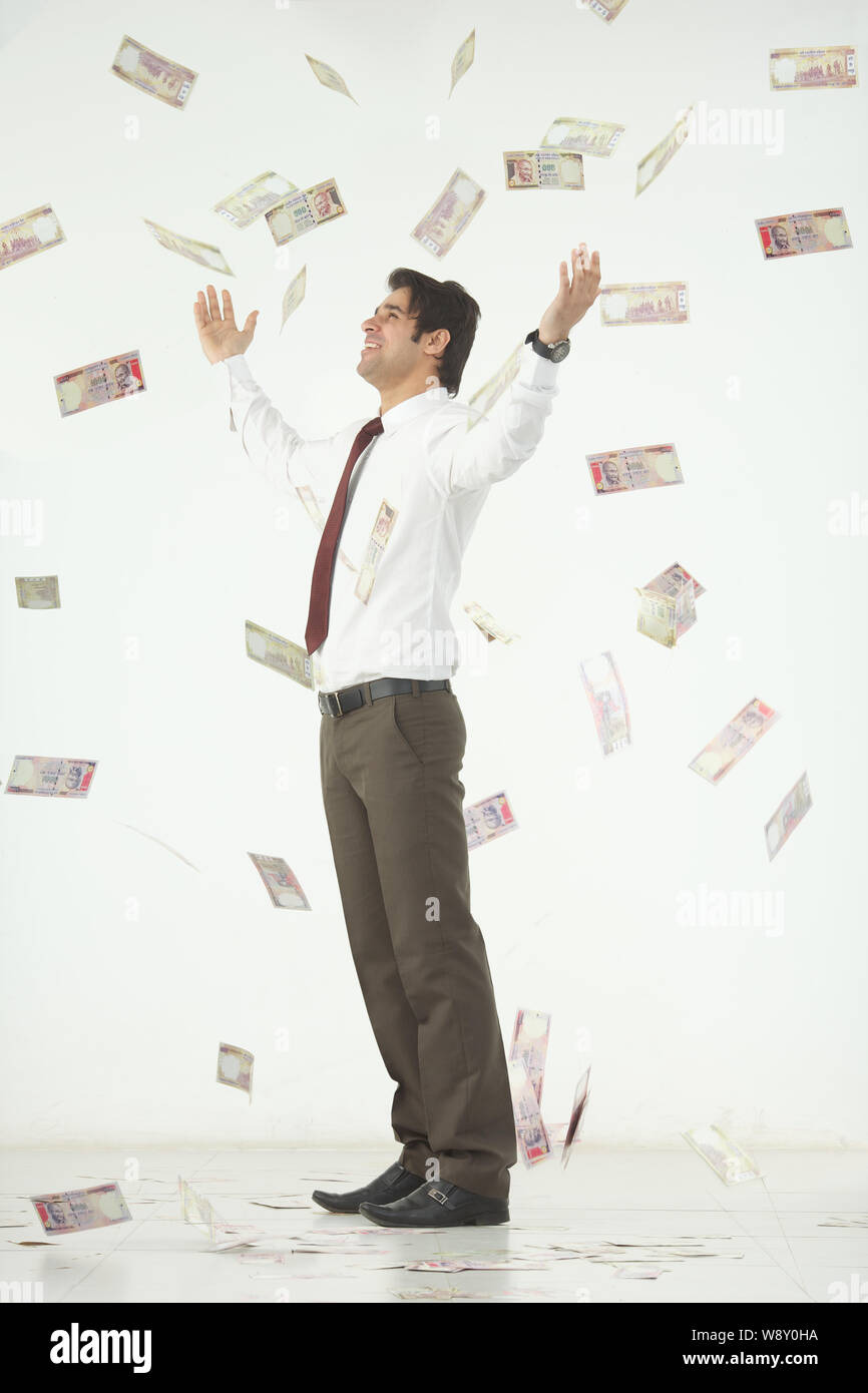 Money falling on a businessman standing with his arms outstretched ...