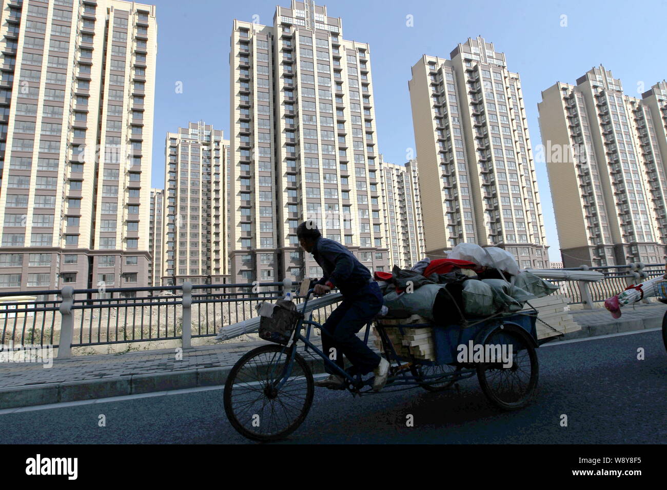 --FILE--A man rides a fully-loaded tricycle past high-rise apartment ...