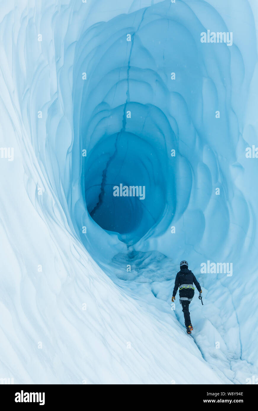 Woman walking toward the shadows of a dark blue ice cave inside the ...