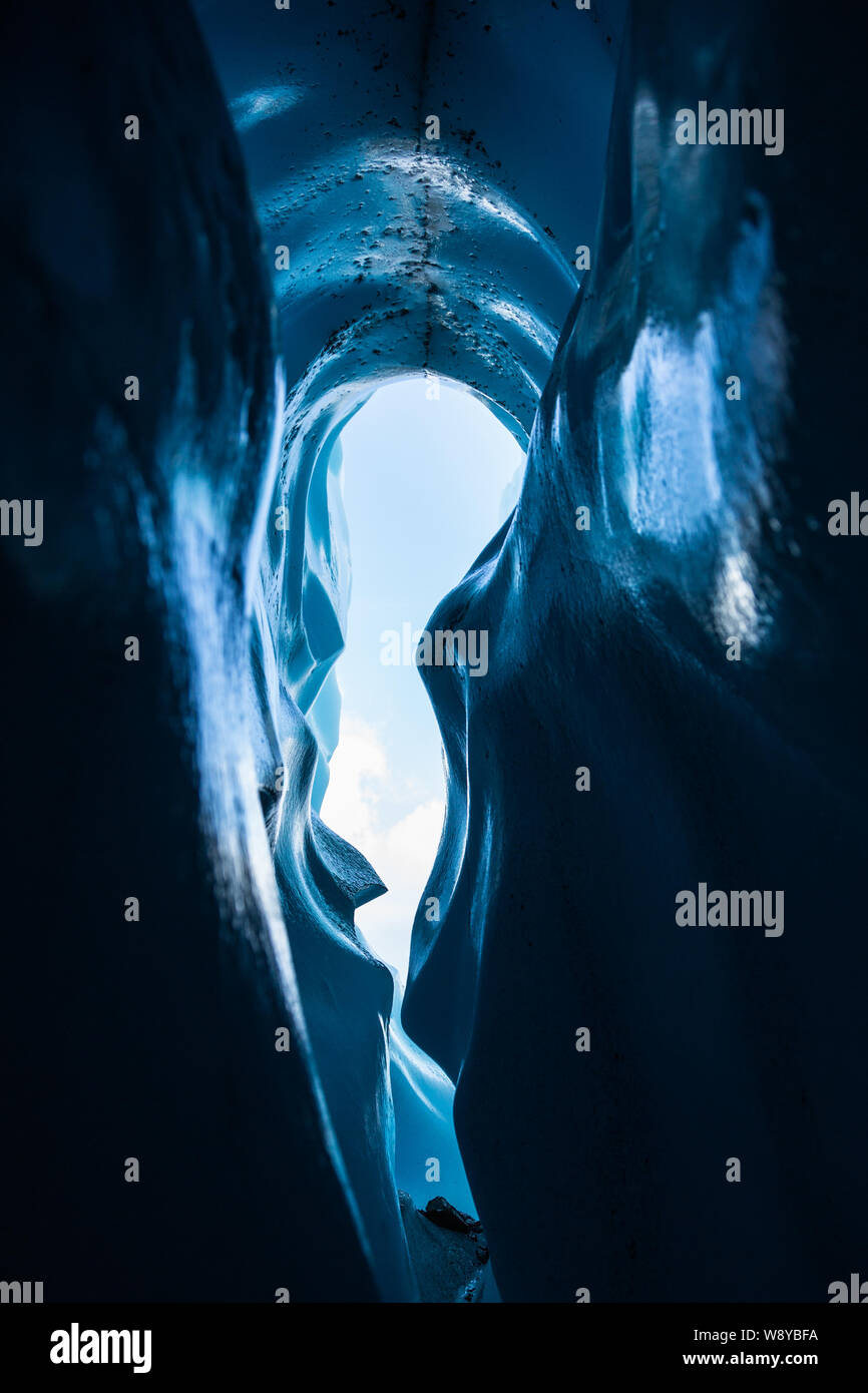 Icy pit of an ice cave, looking up at the sky from deep within a curvy ...