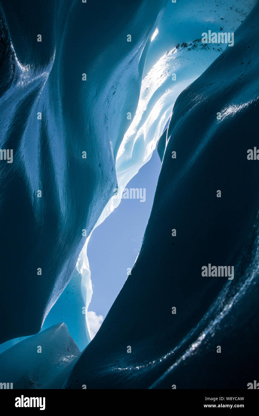 Reflecting smooth ice looking up at the sky from within a deep blue ice ...