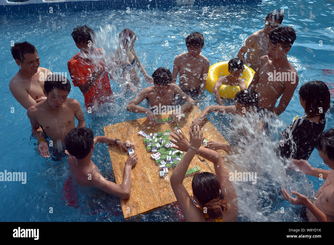 Chinese holidaymakers splash water while watching others play mahjong ...