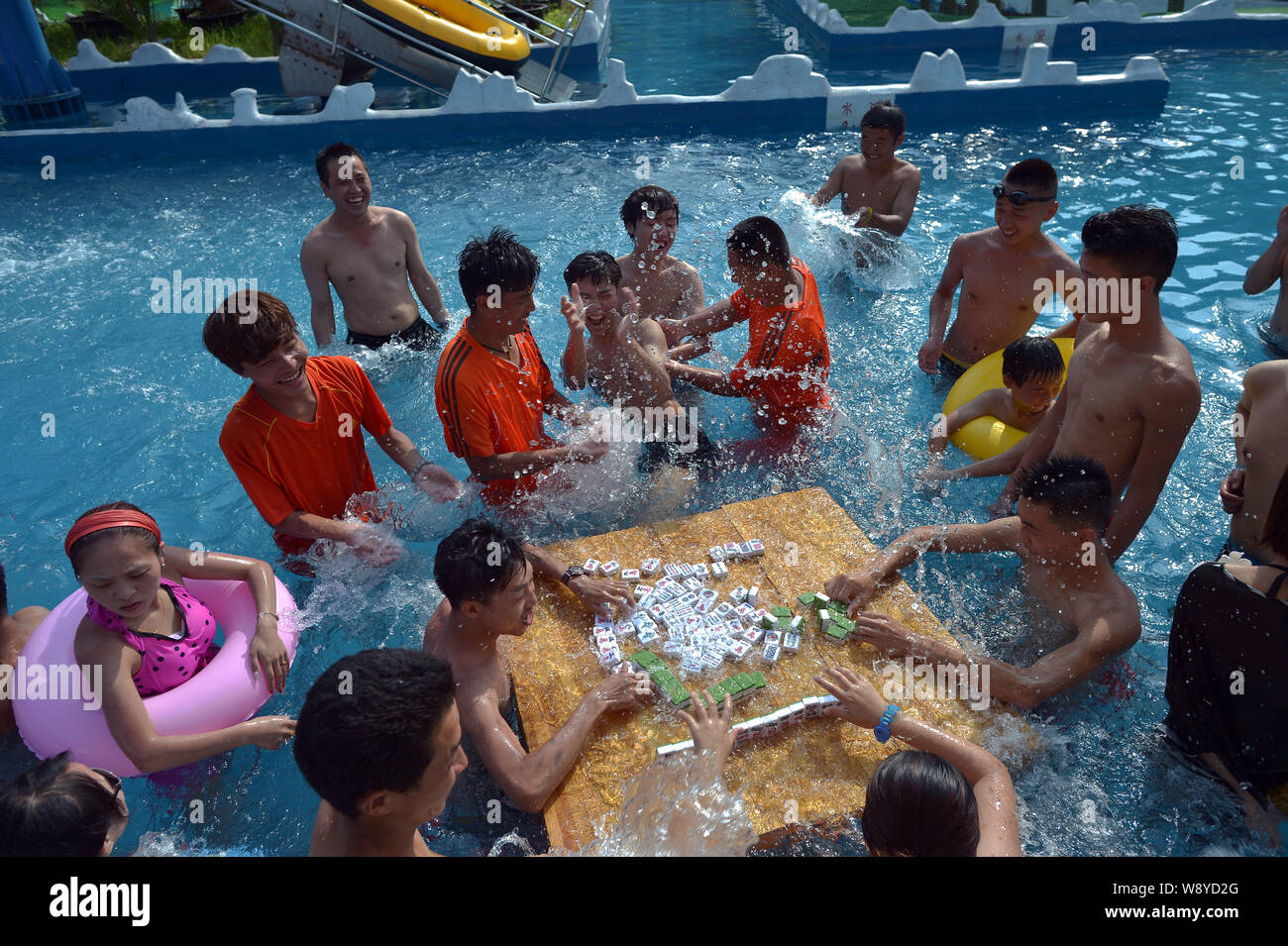Chinese holidaymakers splash water while watching others play mahjong ...