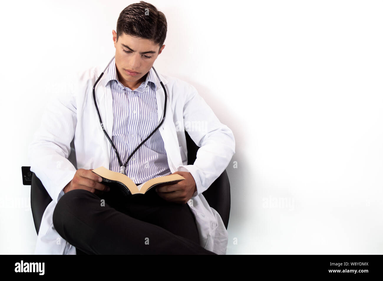 Handsome doctor wearing white lab coat, sitting in chair and reading ...