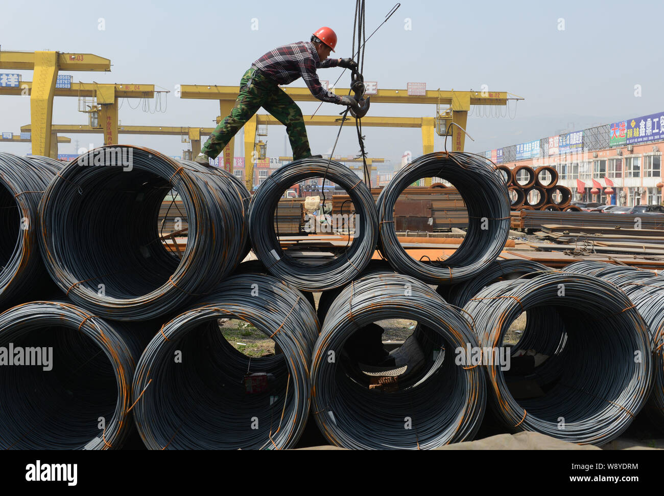 --FILE--A Chinese worker directs a crane vehicle to lift coiled steel ...