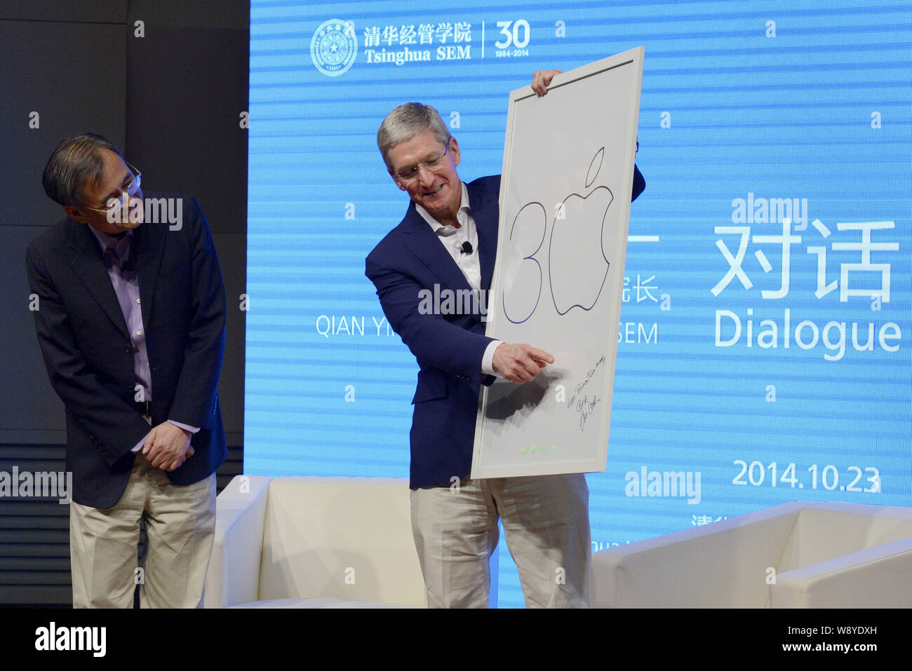 Tim Cook, right, CEO of Apple Inc., shows his autograph on a poster to ...