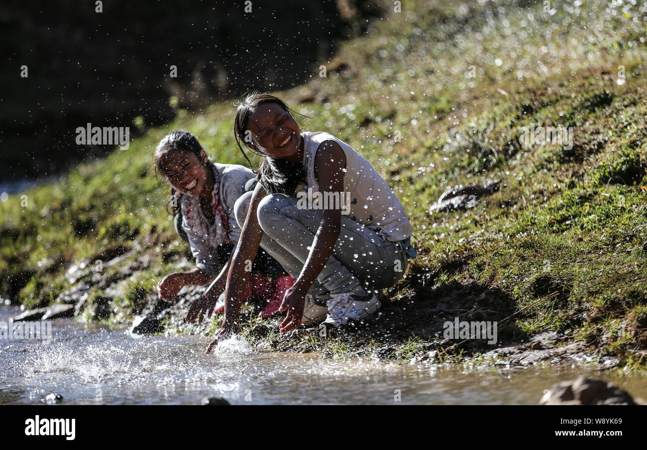 Two young girls have fun by splashing water on the bank of a river in a ...