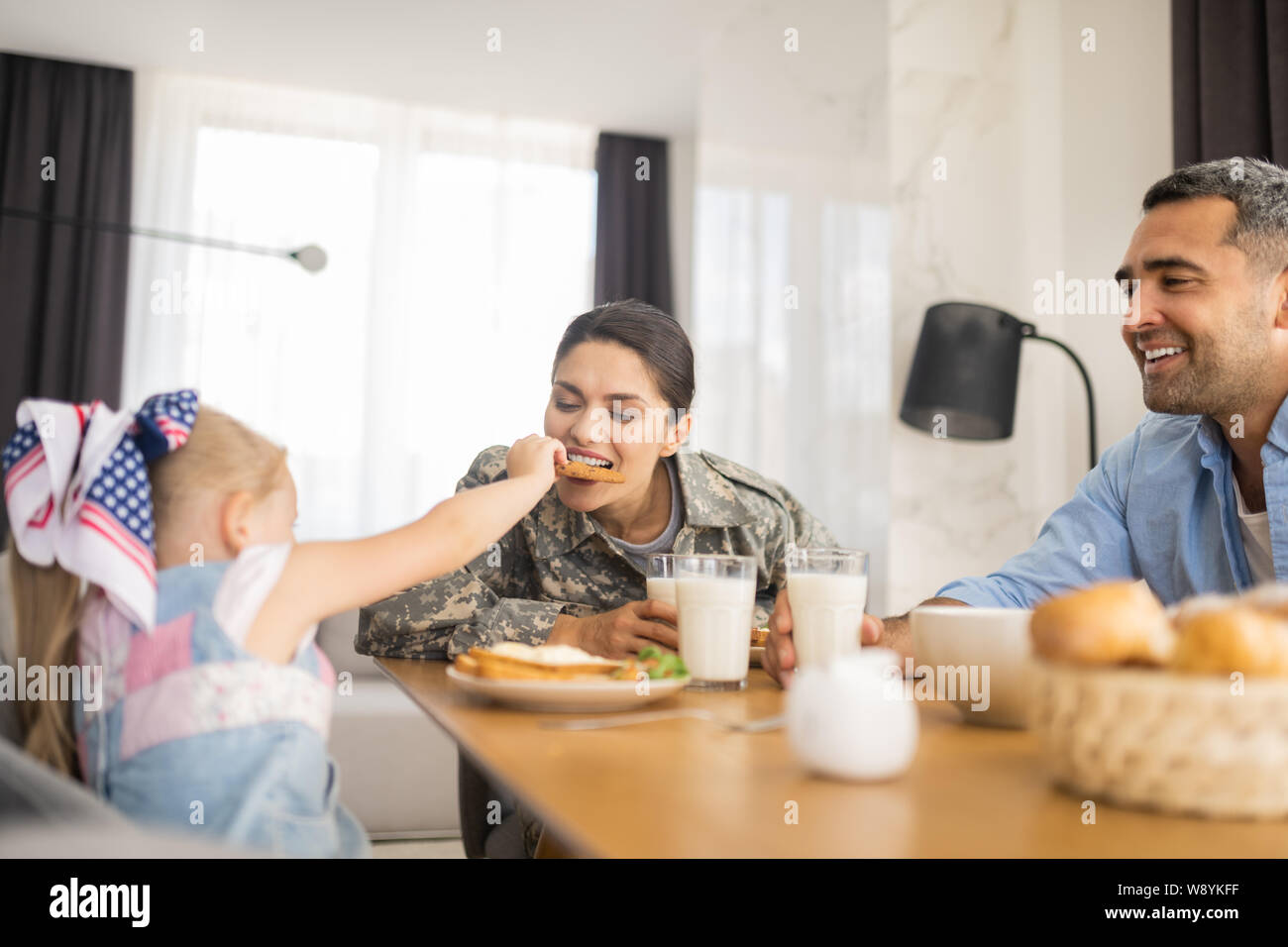 Daughter sharing cookie with mother having family breakfast Stock Photo ...