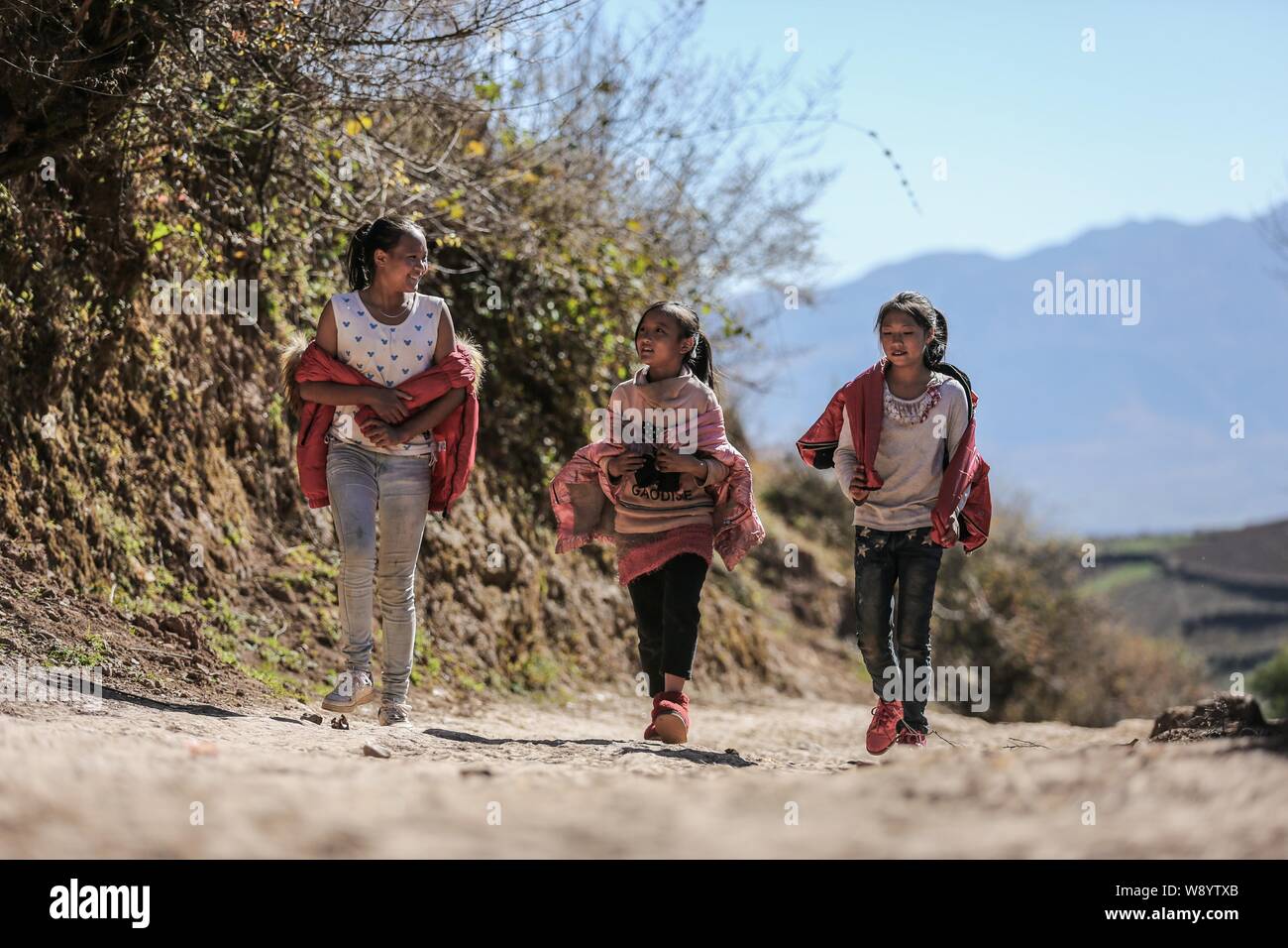 Young girls walk along a mountain road in a poor village in Daliang ...