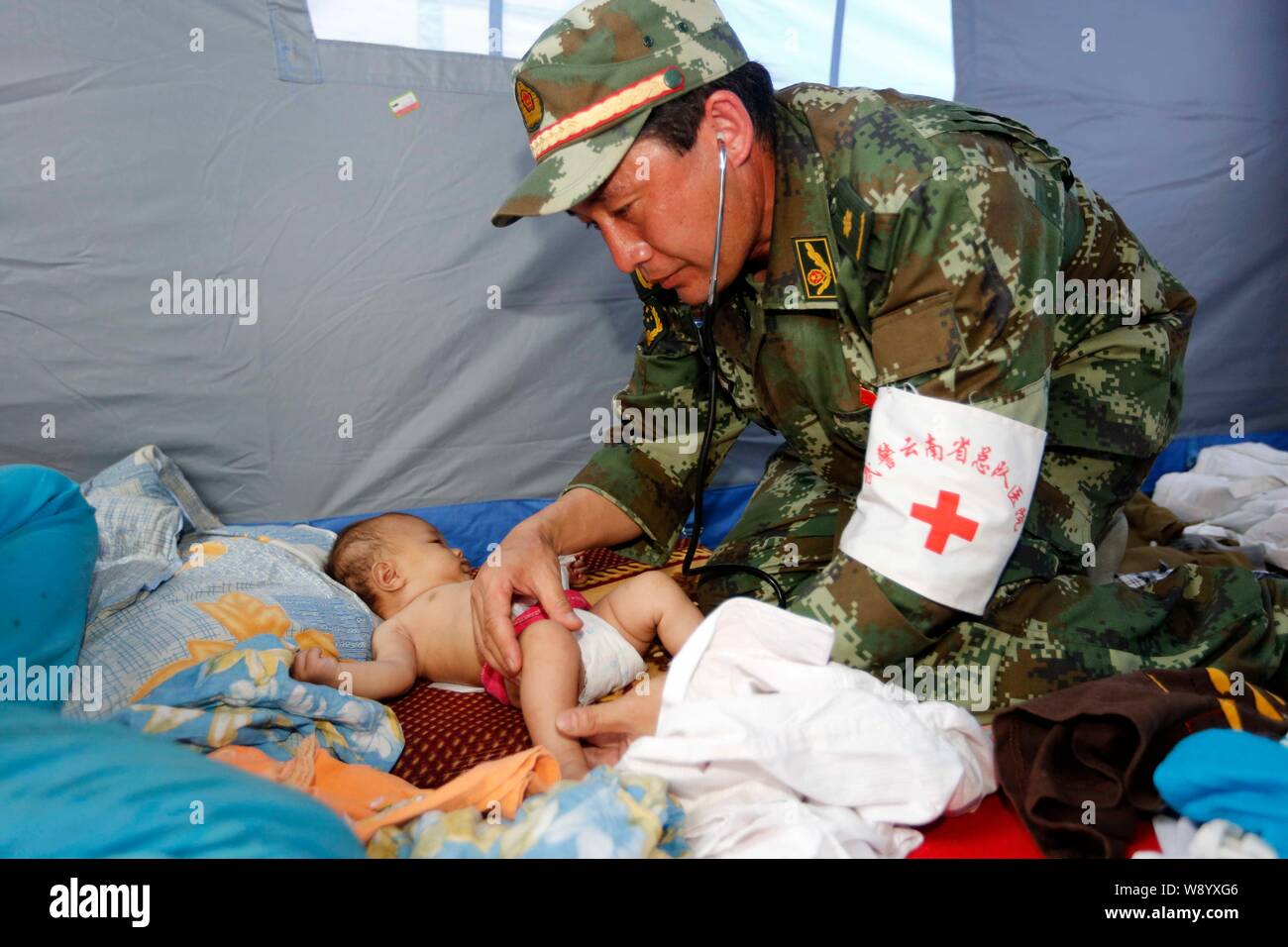 A Chinese rescuer examines an infant at a temporary settlement after ...