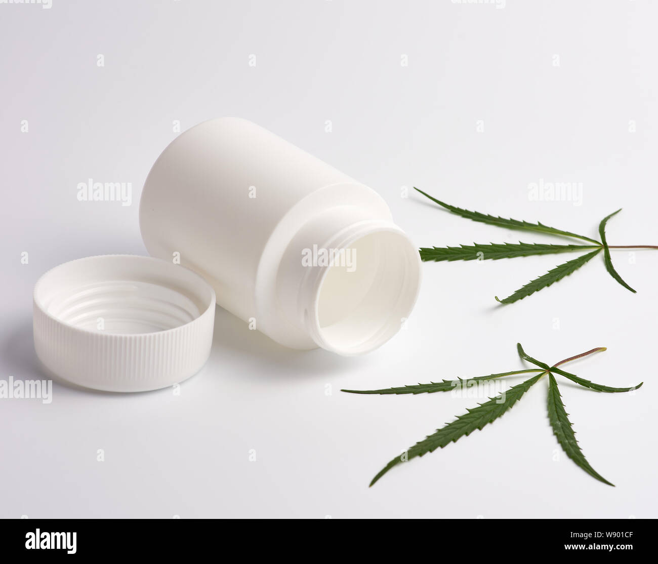 open empty white plastic medical jar for pills and green hemp leaf on a ...